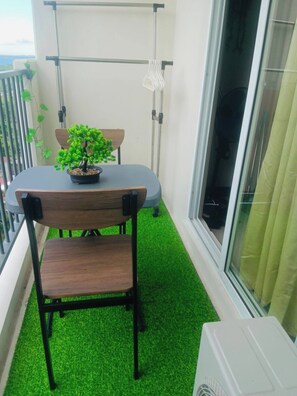 Uma varanda com mesa e cadeiras, um vaso de planta, um lustre pendurado e vista pela janela.