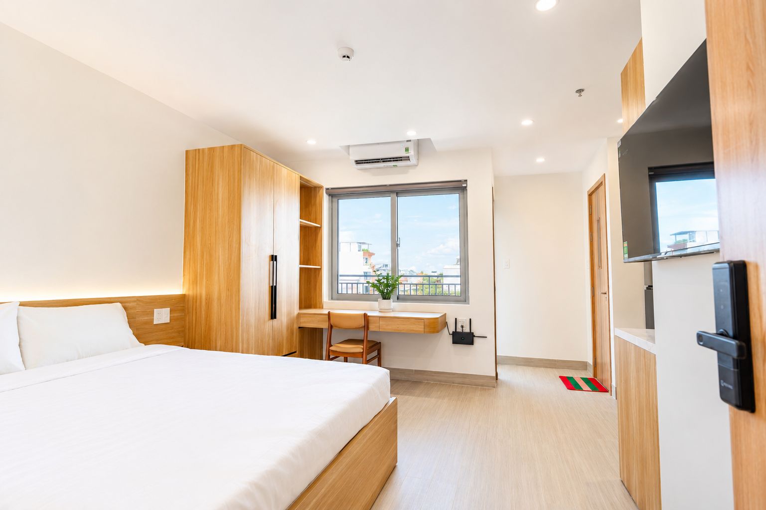 Quarto de hotel moderno com uma cama grande, uma mesa de escritório com cadeira, uma janela com vista e um ar condicionado.
