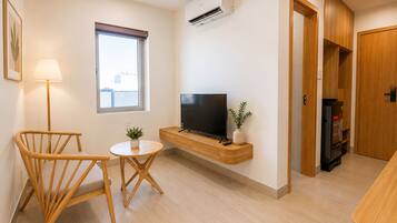 Uma sala de estar moderna com uma TV, uma mesinha, uma cadeira e uma planta.