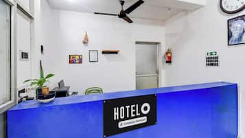 Bancada de recepção de hotel com balcão azul, um relógio e um extintor de incêndio.