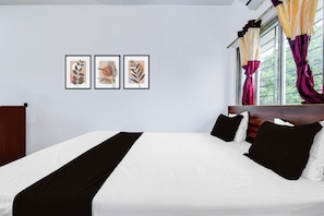 Quarto de hotel com cama, janela com cortinas e três quadros na parede.