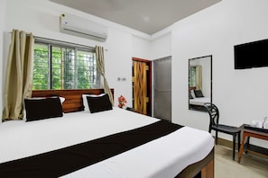 Quarto de hotel com cama grande, ar condicionado, janela com cortinas, espelho e escrivaninha com cadeira.