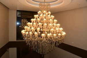 Um lustre grande e ornamentado, com vários níveis e detalhes em cristal, pendurado em um ambiente bem iluminado, com piso espelhado e teto curvo.