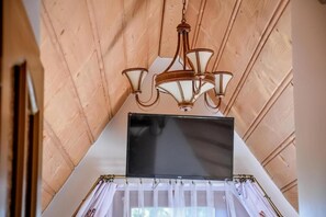 Quarto com lustre, TV de tela plana e janela com cortinas.