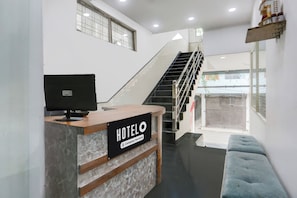 Balcão de recepção de hotel com uma placa, escadas e um banco.