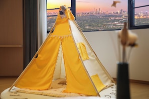 Quarto com uma cama, janela com vista para a cidade e uma estrutura amarela semelhante a uma tenda.