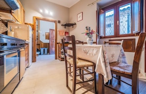 Cozinha equipada com fogão, geladeira e armários de madeira. Há uma  área de jantar com mesa e cadeiras, e uma janela com grades de ferro decorativas.