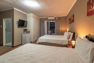 Quarto de hotel com duas camas, televisão, frigorífico e janela com cortinas.