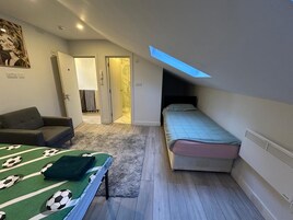 Quarto compacto com cama, sofá, mesinha de centro com tema de futebol e claraboia.