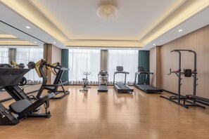 Academia moderna com diversos equipamentos de ginástica, amplas janelas e piso de madeira.