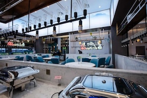 Interior de restaurante com área de bar, mesas e exposição de carros.