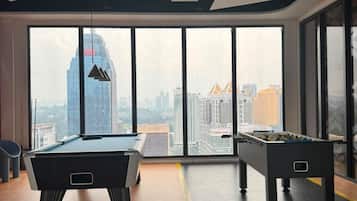Quarto com mesa de bilhar, mesa de futebol de mesa e amplas janelas com vista para a paisagem urbana.
