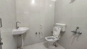 Casa de banho pequena e limpa, com lavatório, sanita e chuveiro, tudo em branco.
