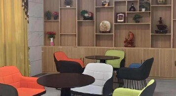 Uma área de estar com diversas cadeiras e uma mesa redonda, rodeada por prateleiras de madeira com objetos decorativos.