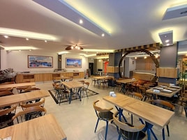 Interior moderno de restaurante com mesas e cadeiras de madeira, área de estar central e um elemento decorativo na parede.