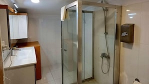 Casa de banho com chuveiro em cabine de vidro, lavatório e sanita.