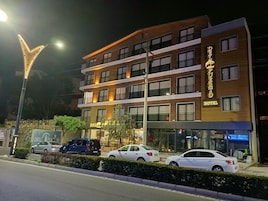 Hotel de vários andares com uma placa chamativa, várias varandas e carros estacionados em frente.
