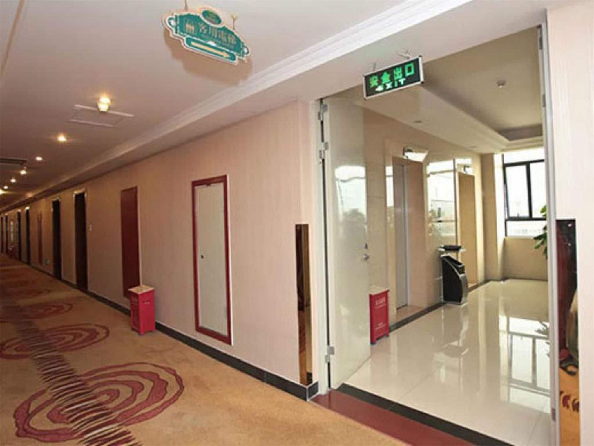 Corredor de hotel com portas, balcão de recepção e placa de saída verde.