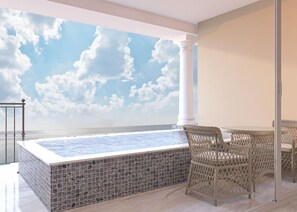 Quarto com grande janela com vista para o mar, hidromassagem, móveis de vime e um pilar branco.