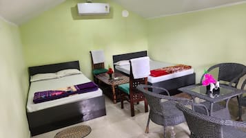 Quarto de hotel com duas camas, uma mesinha, cadeiras de vime e ar condicionado fixado na parede.