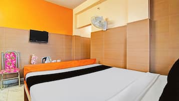 Quarto de hotel com cama, uma cadeira, televisão fixada na parede e uma mesinha com chaleira e chávenas.