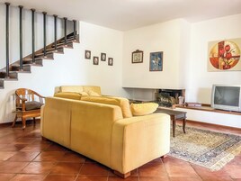 Uma sala de estar com sofá, uma cadeira de madeira, lareira, televisão e escada.