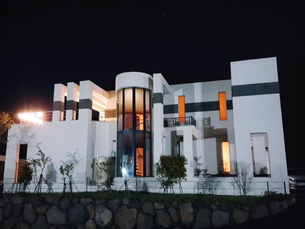 Um edifício moderno com uma seção central cilíndrica, várias varandas e uma parede de pedra em primeiro plano.