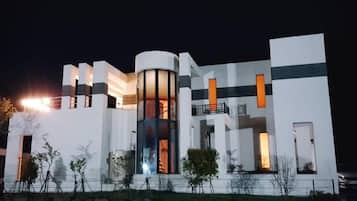 Um edifício moderno com uma seção central cilíndrica, várias varandas e uma parede de pedra em primeiro plano.