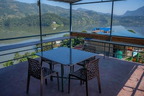 Terraço com mesa e cadeiras com vista para um lago e colinas.