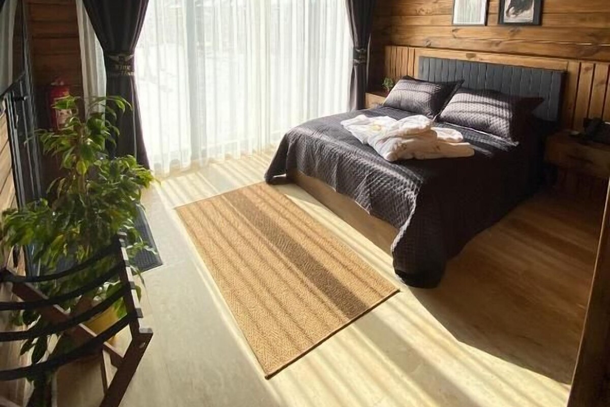 Quarto com painéis de madeira, uma cama, uma cadeira e uma planta.