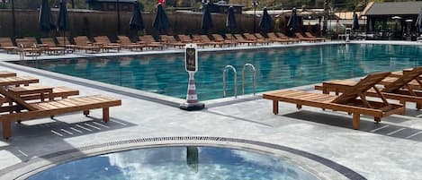 Área de piscina em resort com espreguiçadeiras, hidromassagem e vista para uma encosta arborizada.