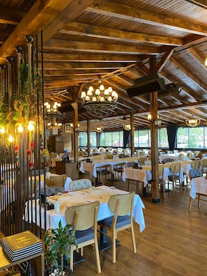 Restaurante com vigas de madeira, lustres e mesas preparadas para refeições.