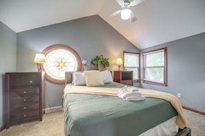 Quarto com cama, penteadeira, mesa de cabeceira, luminária, janela e ventilador de teto.