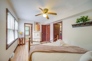 Quarto com cama, ventilador de teto, cômoda, espelho e janela com persianas.