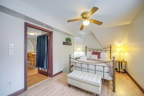 Quarto com cama, luminárias de cabeceira, ventilador de teto e uma pequena mesa com livros.