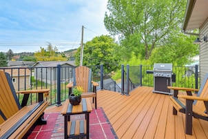 Um deck de madeira com móveis para área externa, churrasqueira e vista para um bairro residencial com casas e árvores.