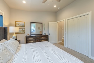 Quarto com cama, penteadeira e porta que dá para outro cômodo.