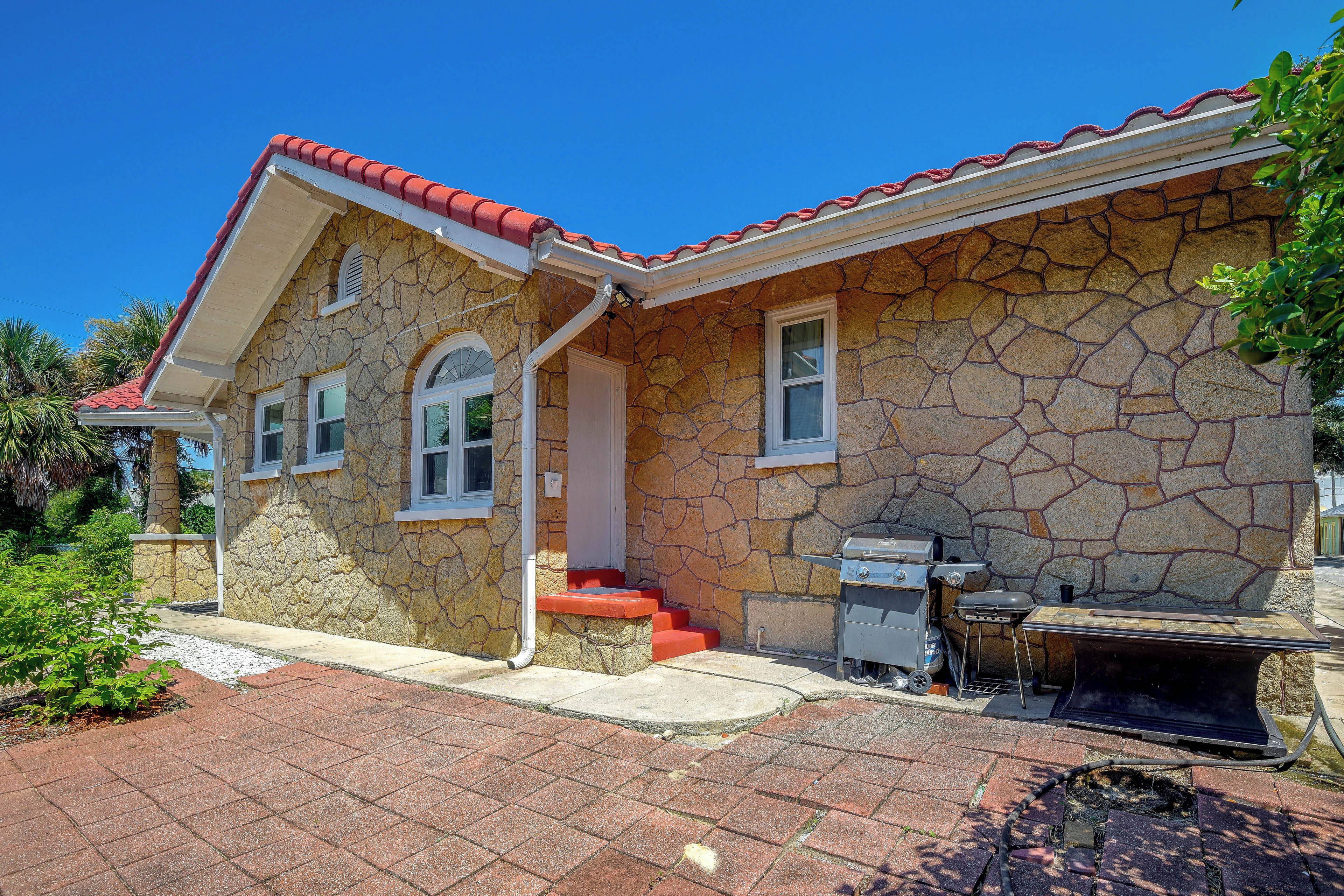 Uma casa de pedra com telhado vermelho, varanda frontal e churrasqueira.