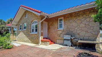Uma casa de pedra com telhado vermelho, varanda frontal e churrasqueira.