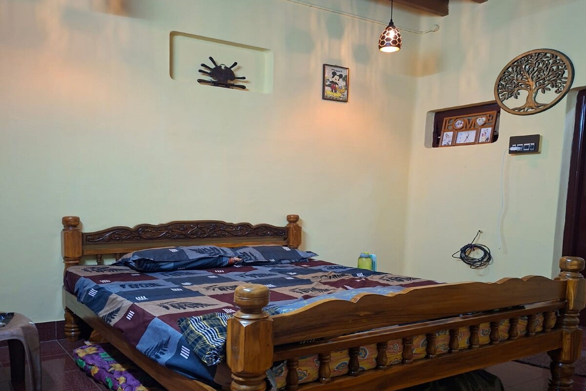Quarto com cama de madeira, um banquinho pequeno, almofada colorida, relógio e decoração na parede.