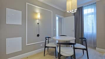 Uma área de refeições com uma mesa redonda e quatro cadeiras, uma luminária fixada na parede e uma porta que dá para outro cômodo.