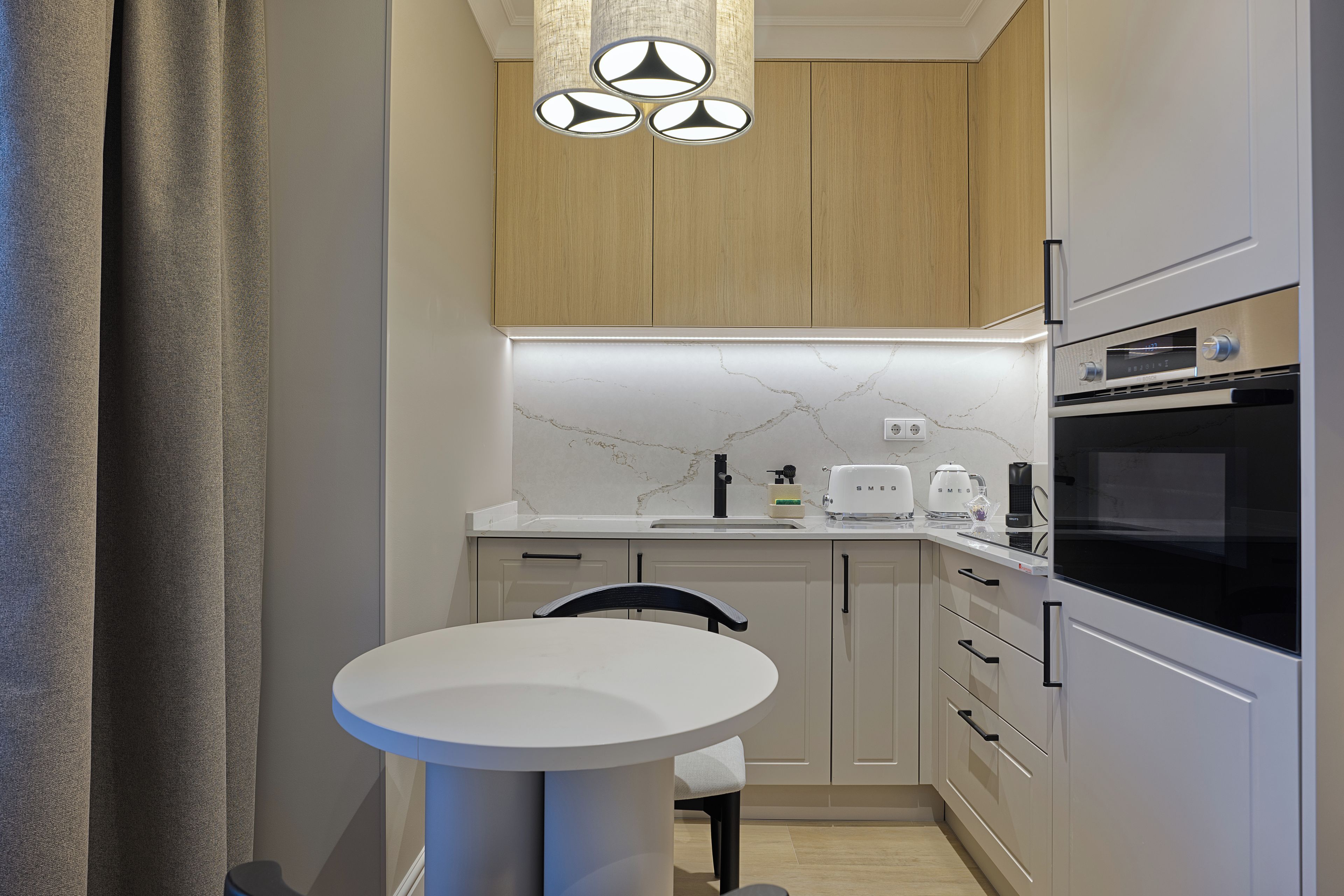 Cozinha moderna com bancada branca, forno embutido e luminária pendente.