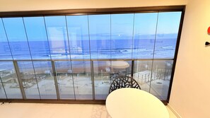 Quarto com grande janela com vista para o oceano, uma cadeira branca e uma pequena mesa.