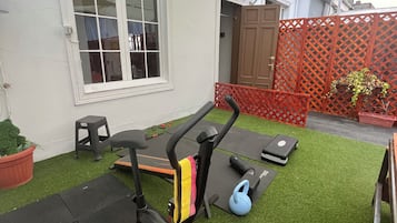Espaço de ginástica em casa com equipamentos de exercício, uma janela e uma porta.