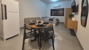 Um espaço de estar compacto com cozinha compacta, área de refeições com mesa redonda e cadeiras, cama com janela e TV na parede.