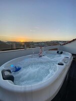 Banheira de hidromassagem em terraço com vista para a cidade ao pôr do sol.