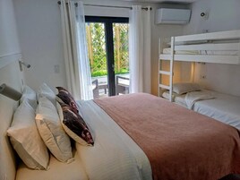 Quarto com cama, beliche, janela com cortinas e aparelho de ar condicionado.
