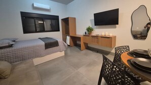 Quarto com cama, escrivaninha, cadeira, mesa de jantar, televisão e espelho.