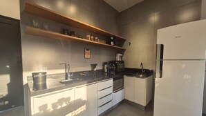 Cozinha moderna com geladeira, forno, cafeteira e prateleira com utensílios de cozinha.
