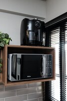 Cozinha com máquina de café preta e micro-ondas em prateleira de madeira.